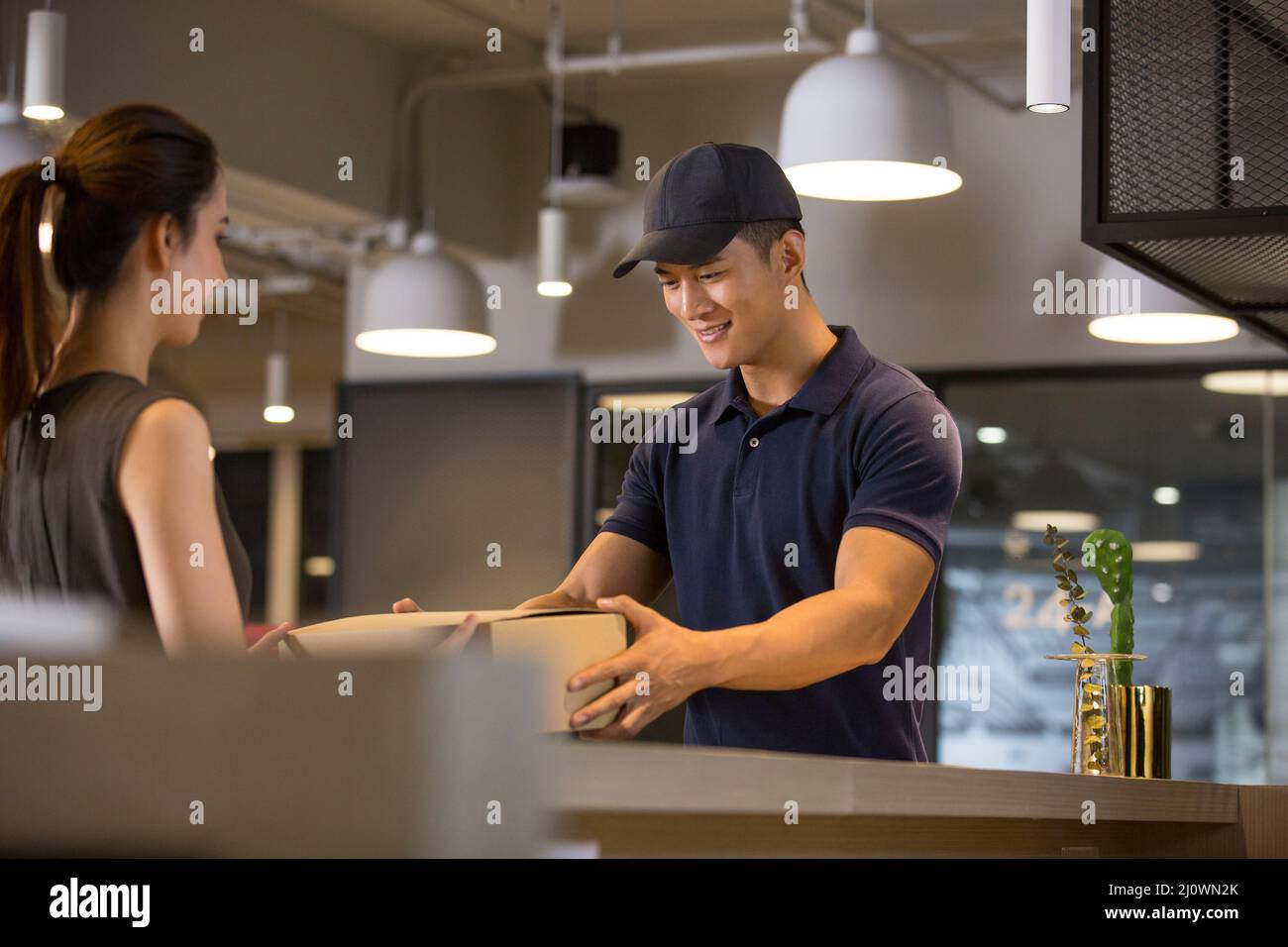 Chinese delivery man handing box to receptionist Stock Photo - Alamy