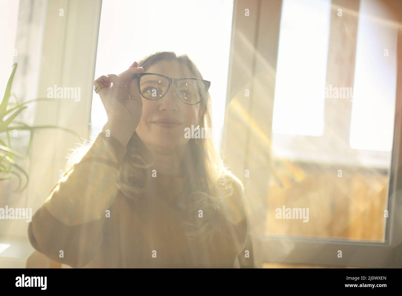 Happy middle-aged blonde woman holding glasses while sitting in room ...