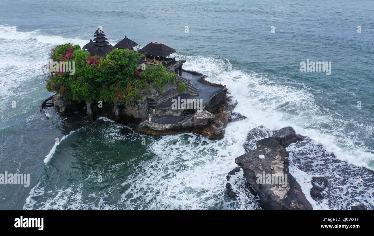 Strong ocean waves crashing into rocky cliff with Tanah Lot temple in ...