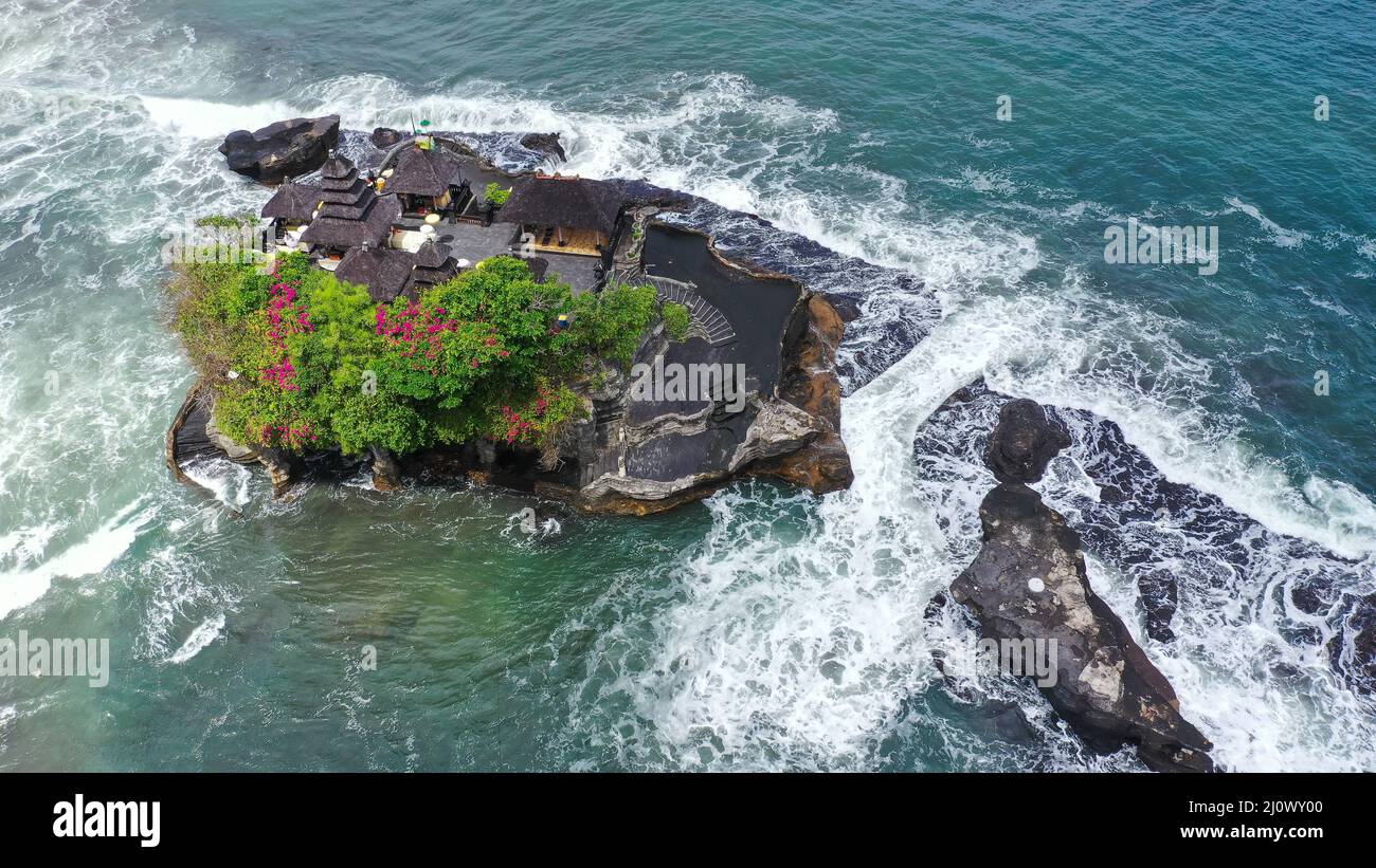 Strong ocean waves crashing into rocky cliff with Tanah Lot temple in ...