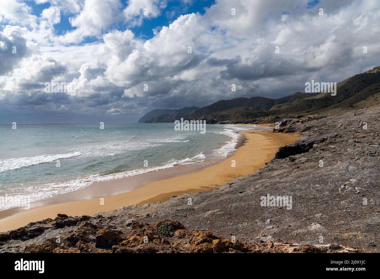 A rocky ocean coast with mountains and a beautiful golden sand beach in ...