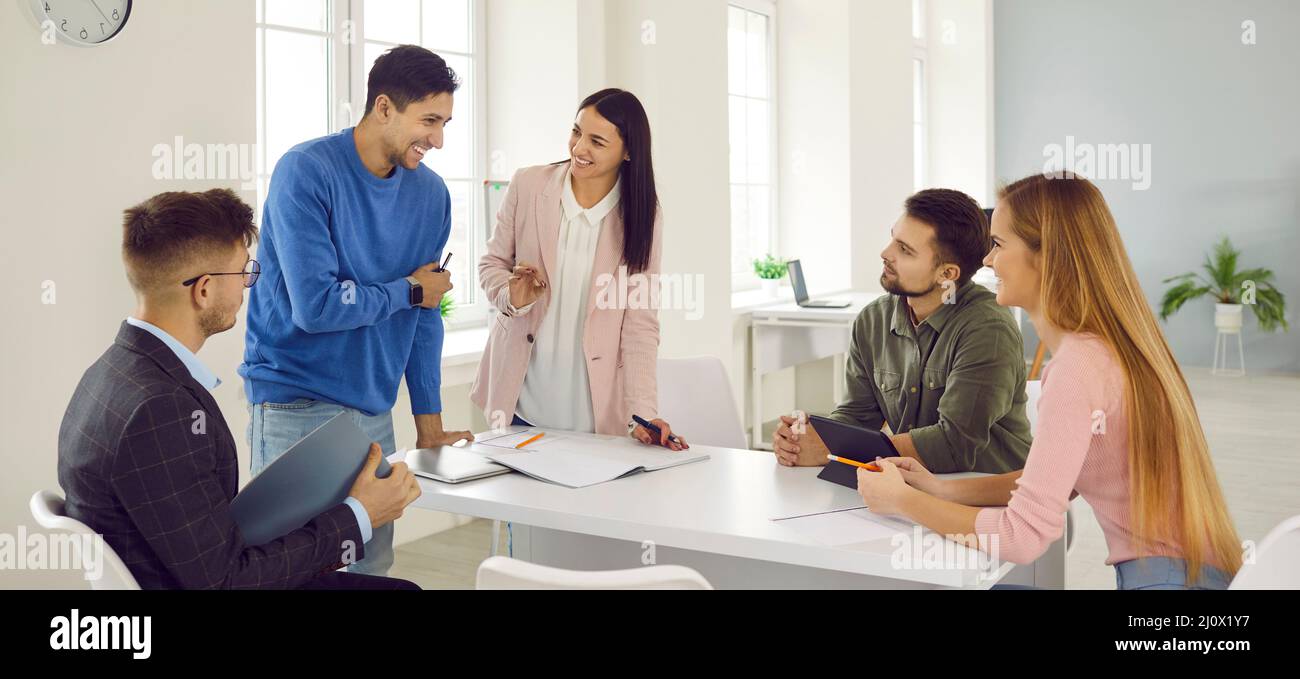 Smiling young workers sitting at office desk, talking and discussing ...