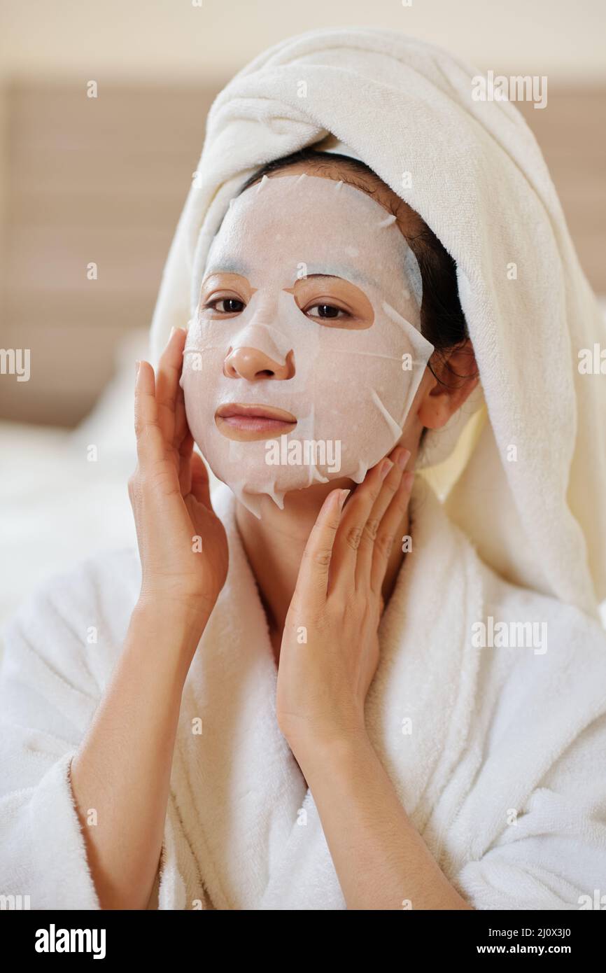 Portrait of positve young woman applying soothing and hydrating sheet ...