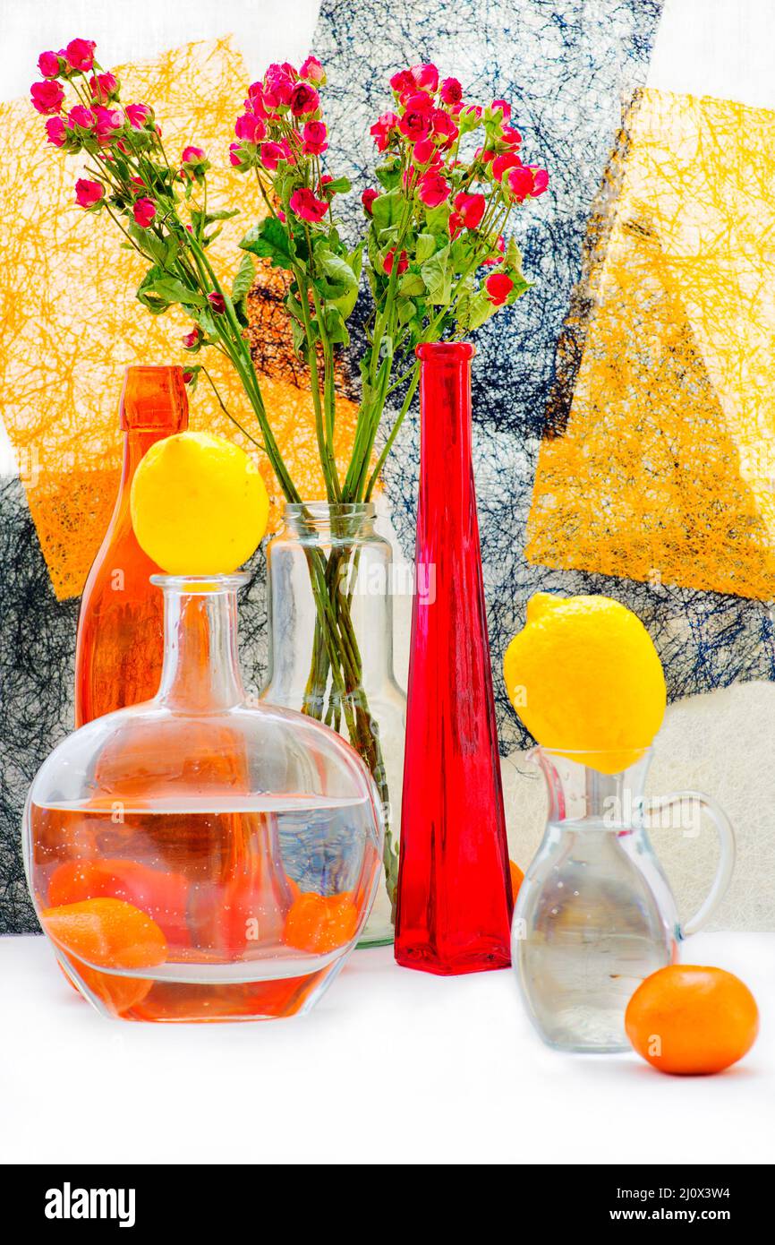 Still-life with colored glassware, branch of roses, lemons and ...