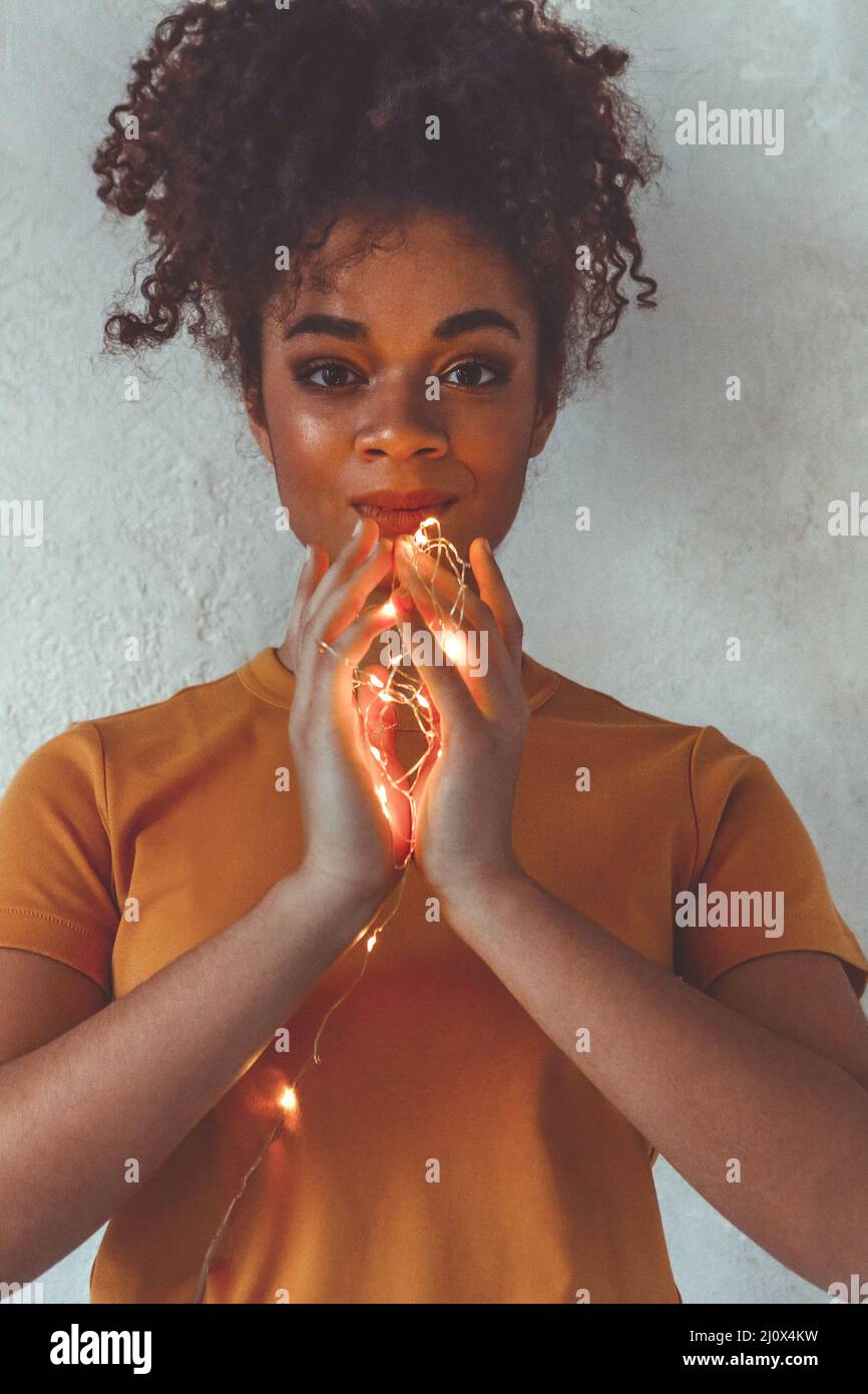 Happy african american girl standing with festive led lights around ...