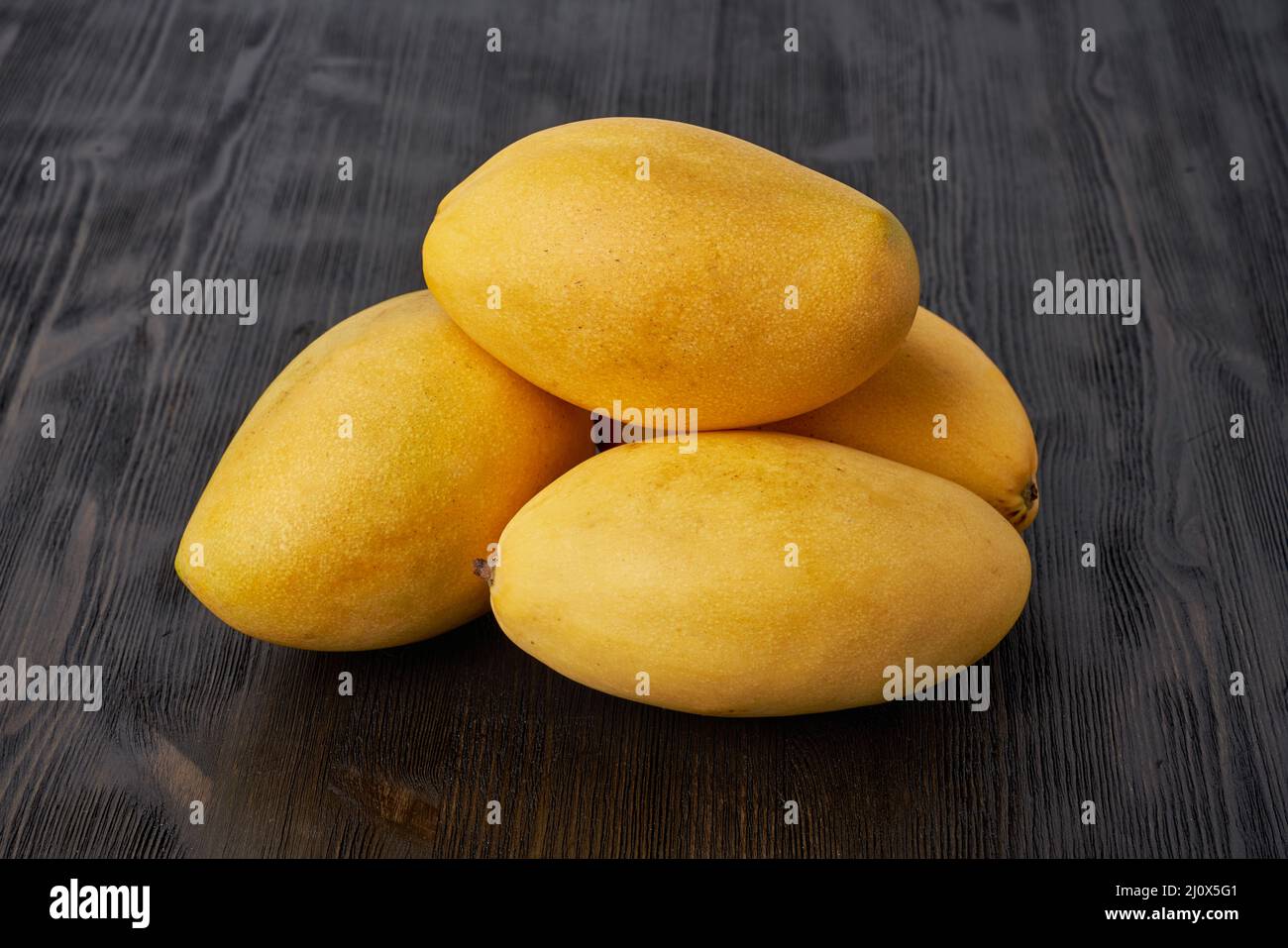 Four whole fruit mangoes on wooden table. Large juicy bright ripe ...