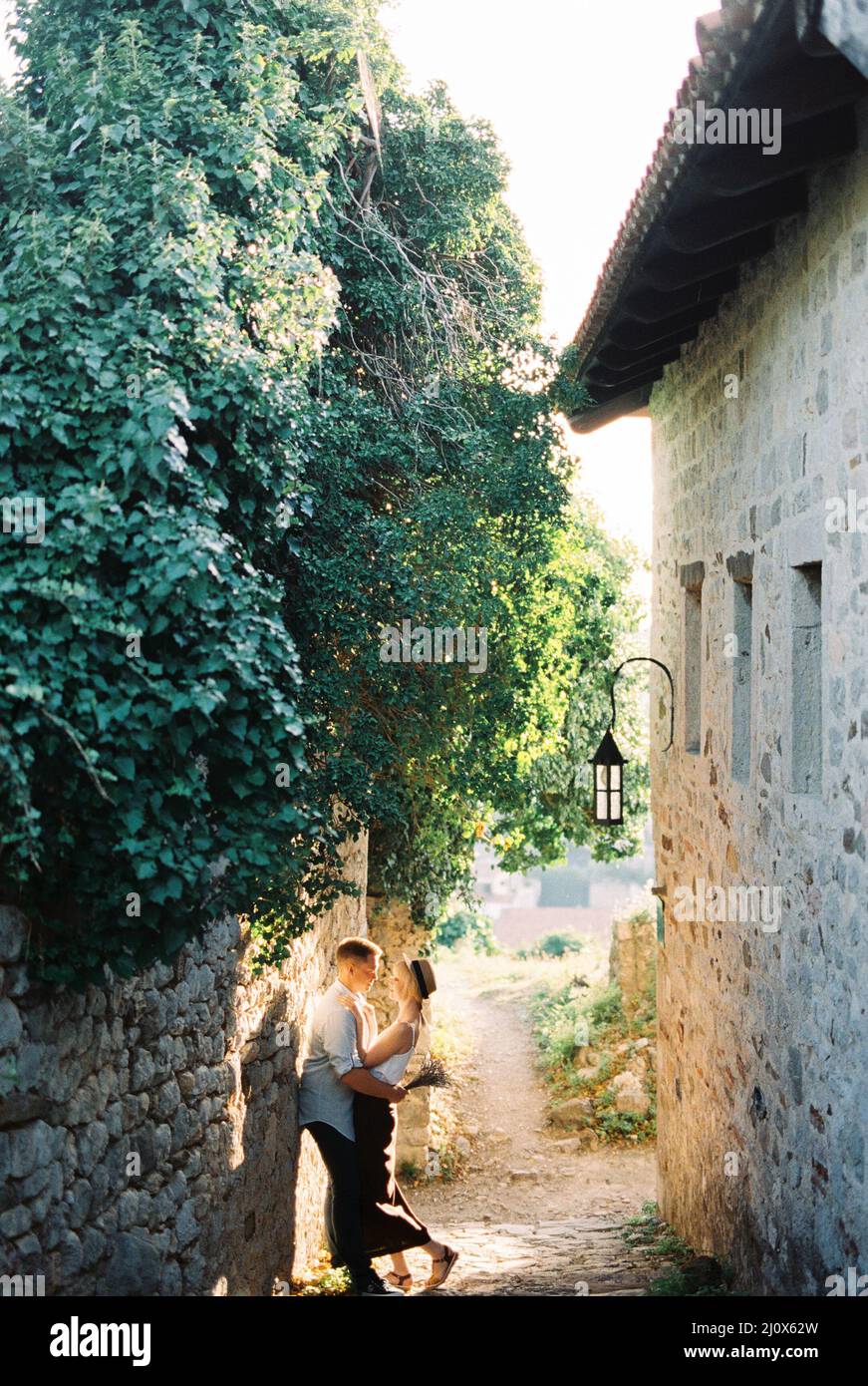 Man hugs a woman near a stone wall in a narrow street of an old town ...