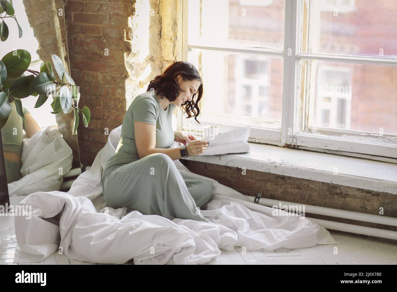 Young brunette woman relaxing at home alone reading favorite magazine ...
