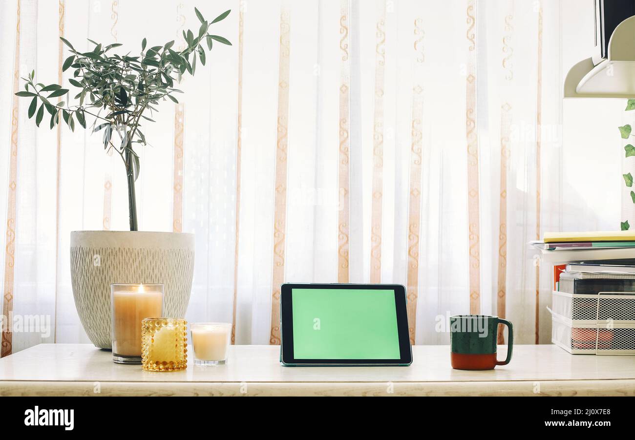 Digital tablet with green screen on table with houseplant, candles and ...