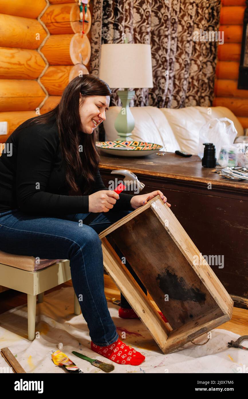 Caucasian smiling lady fixing old box made of wood with help of hammer ...