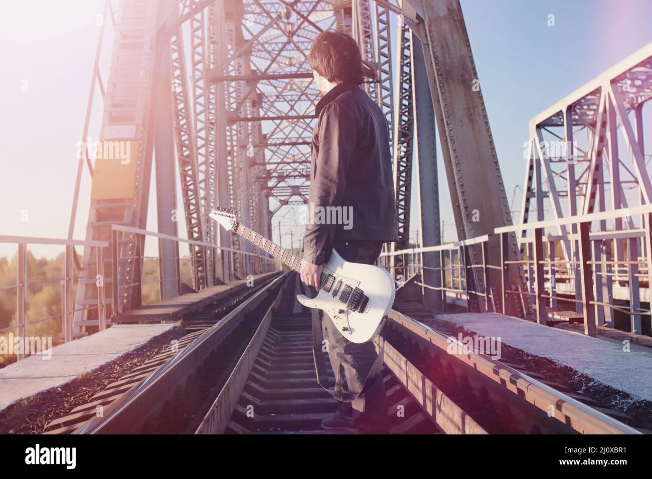 A man with an electric guitar on the railway. A musician in a leather ...