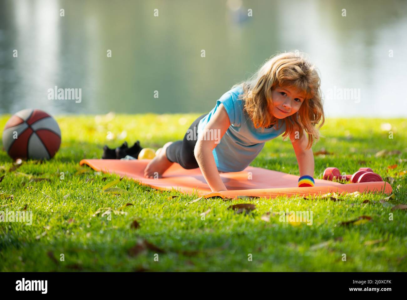 Child is pushing up on the green meadow, working out wearing sportswear ...
