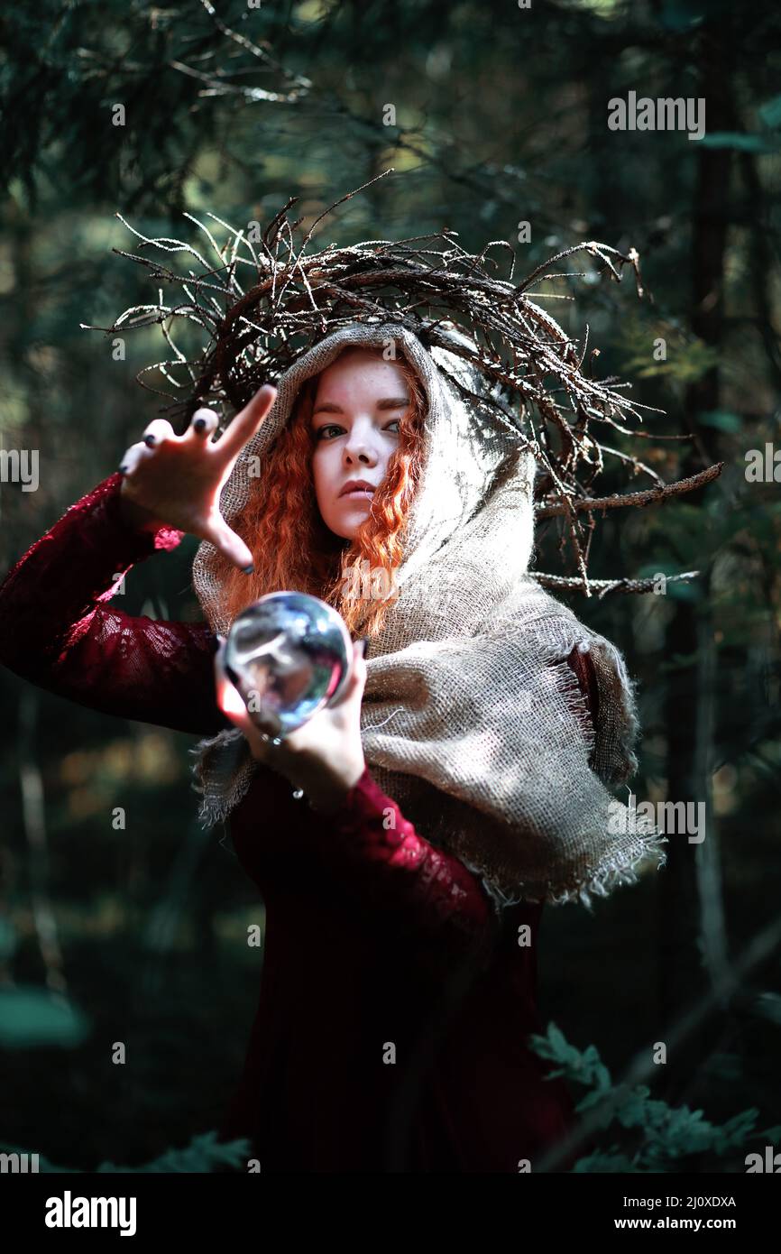 The red-haired witch holds a ritual with a crystal ball in the forest ...