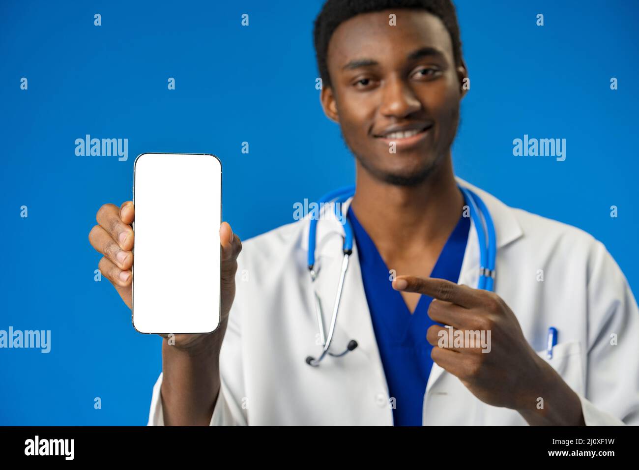 Cheerful african doctor using mobile phone over blue studio background ...