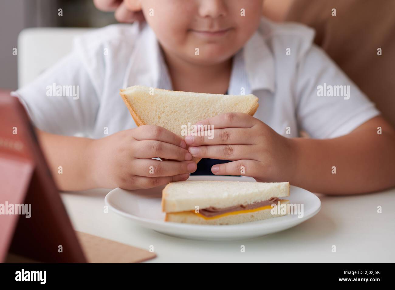 Cropped image of little boy eating tasty sandwich with ham and cheese ...