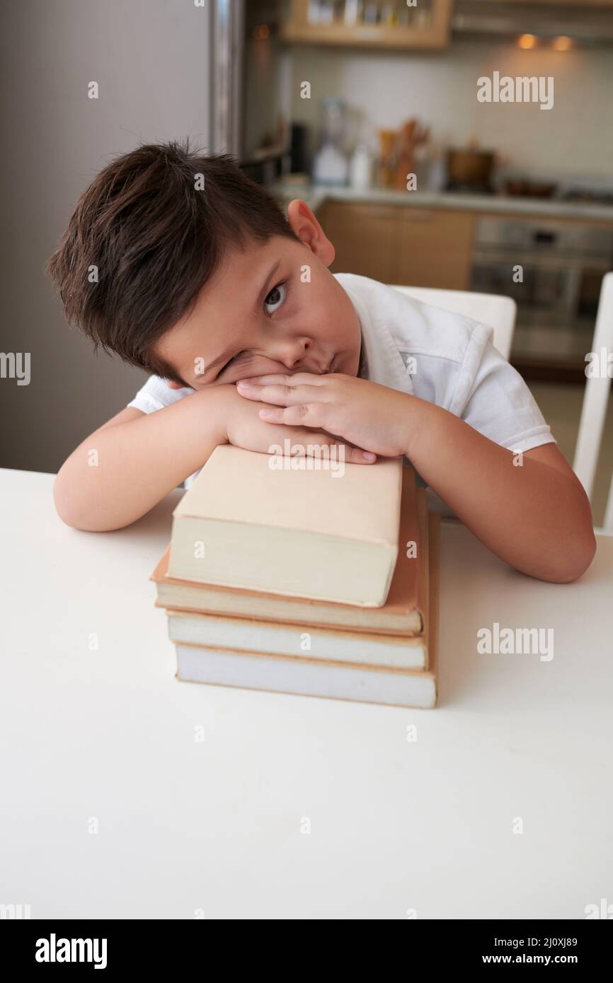 Tired and bored little boy leaning on stack or school books and looking ...