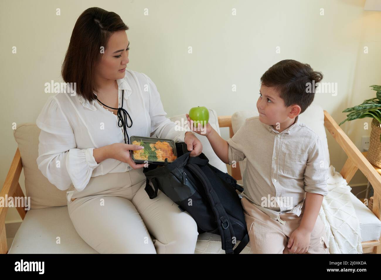 Mother and son putting container with school lunch and snacks in school ...