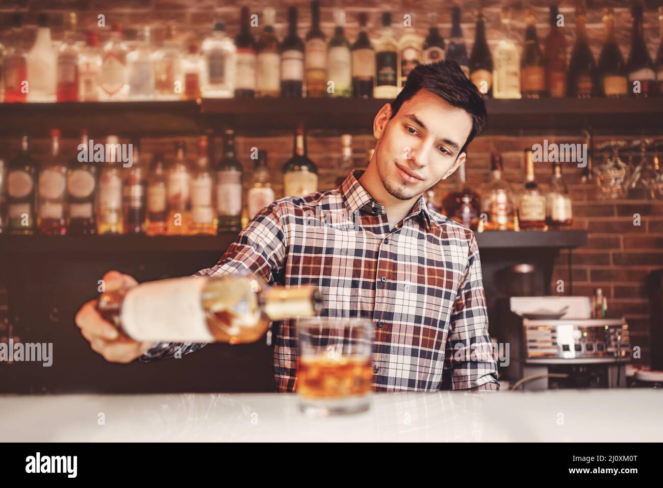 Barman pours whiskey from bottle into glass of ice bar. Dark brown ...