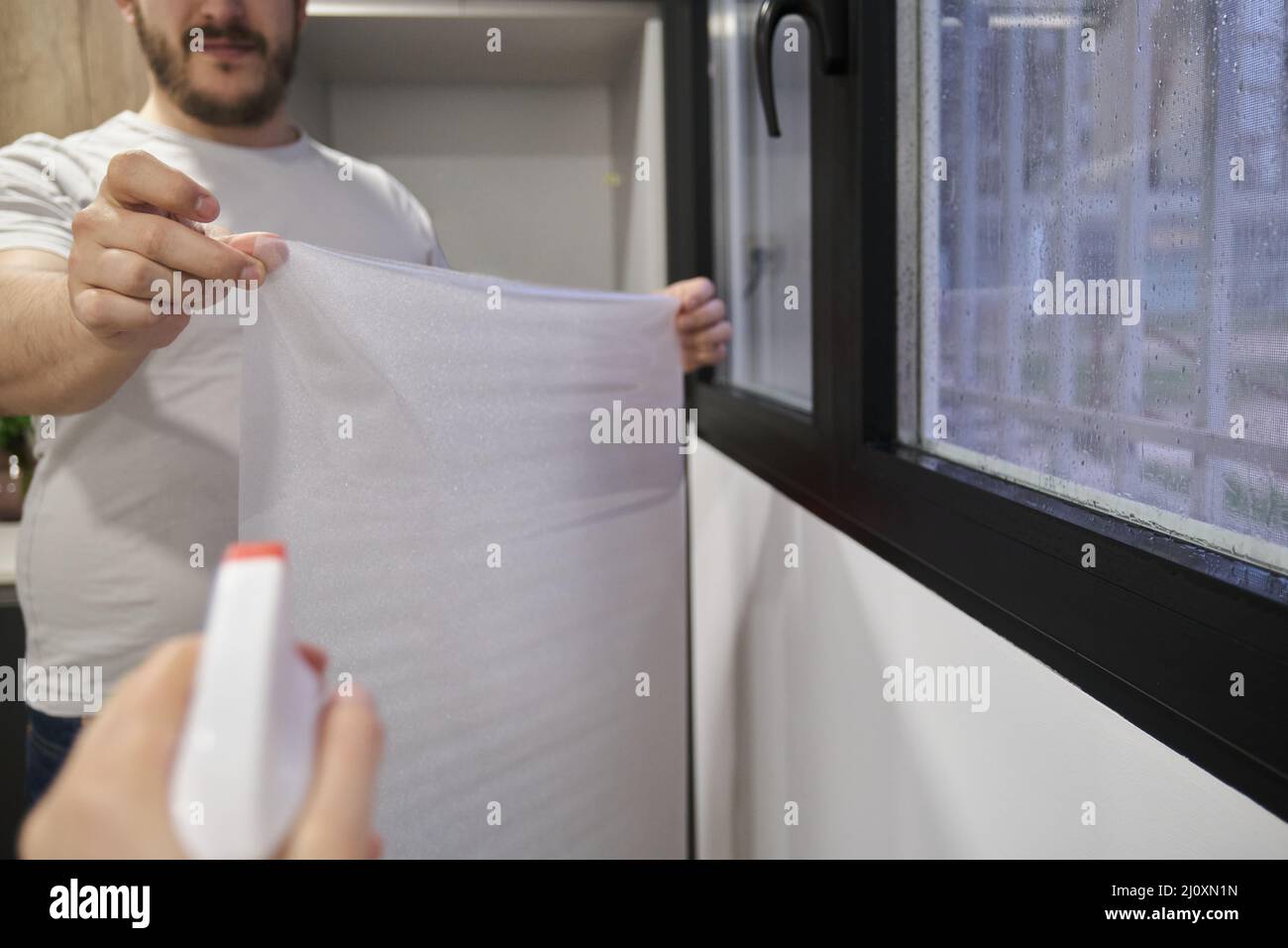 Man spraying frosted window vinyl with water to install it on window ...