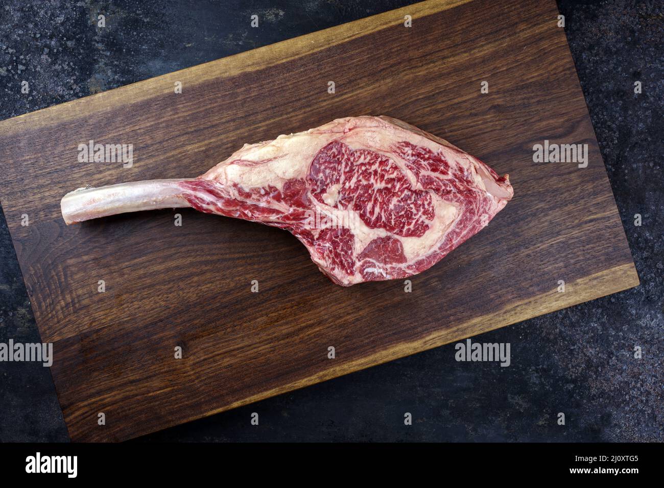 Raw dry aged wagyu tomahawk steak offered as top view on a wooden ...
