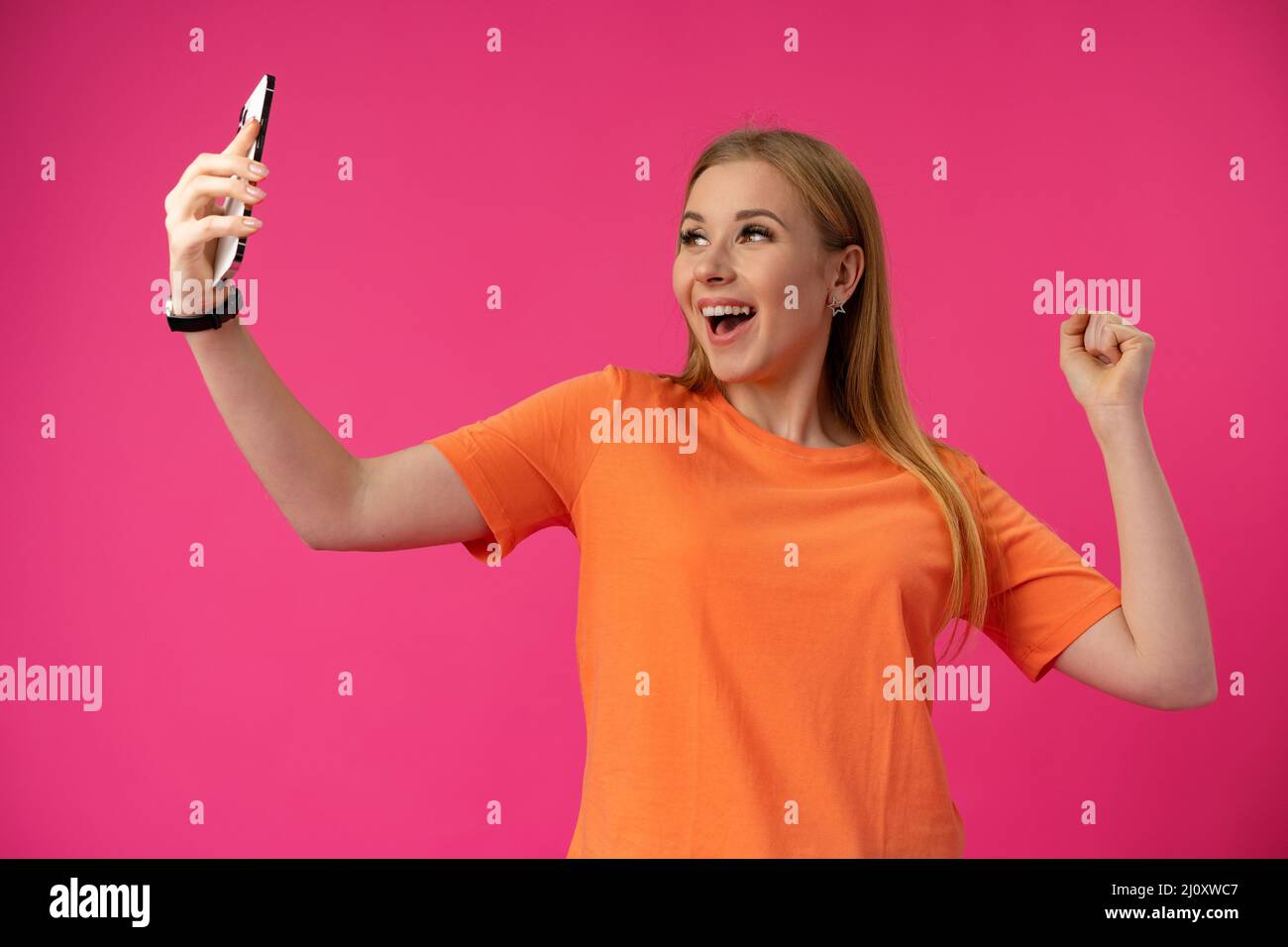 Excited surprised young woman using mobile phone against studio ...