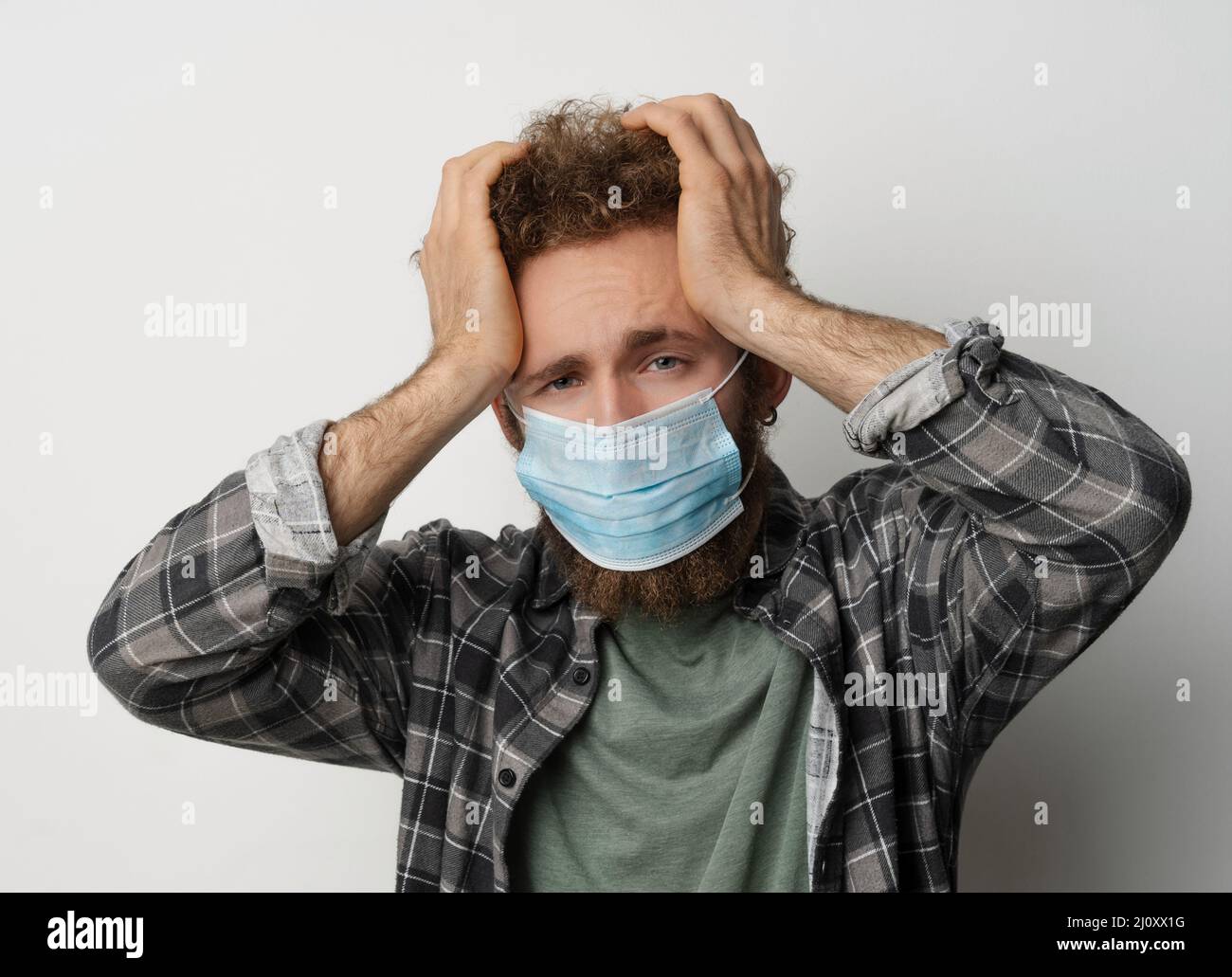 Sick young man in medical face mask feel migraine holding head ...