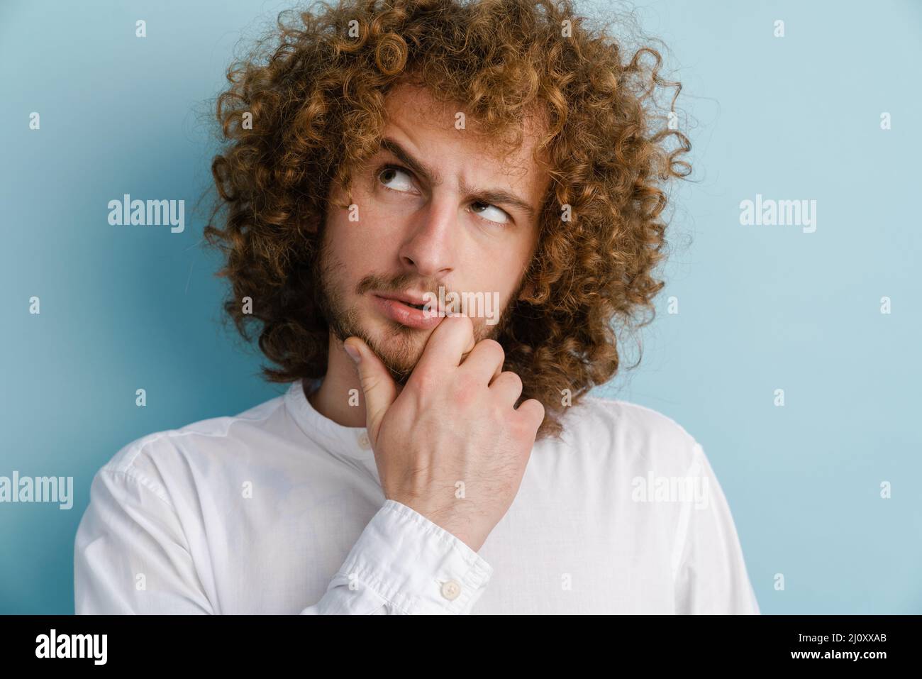 Young man with ginger curly hair frowning and looking aside isolated ...