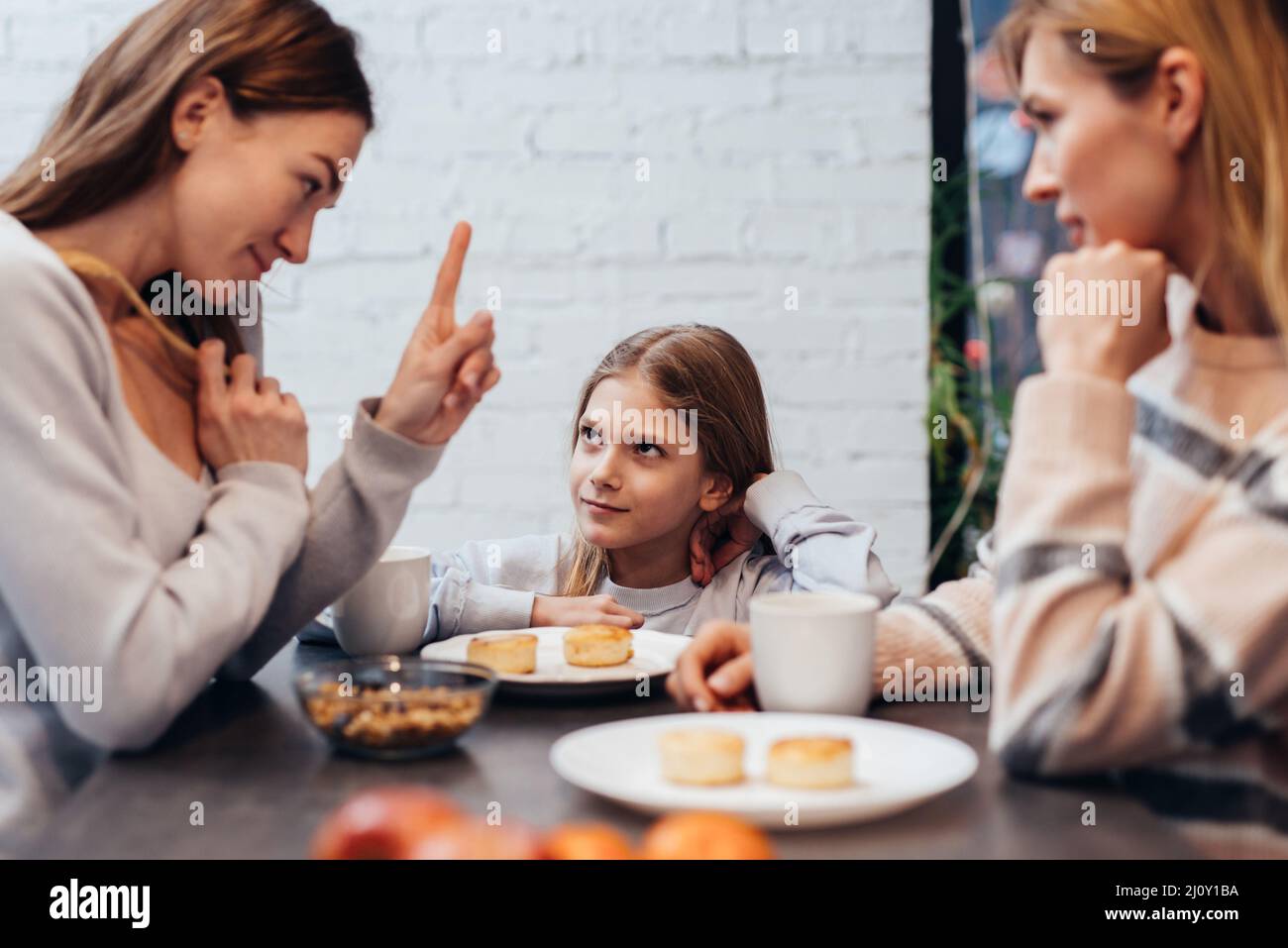 Female friends and little girl sitting together at the kitchen table ...