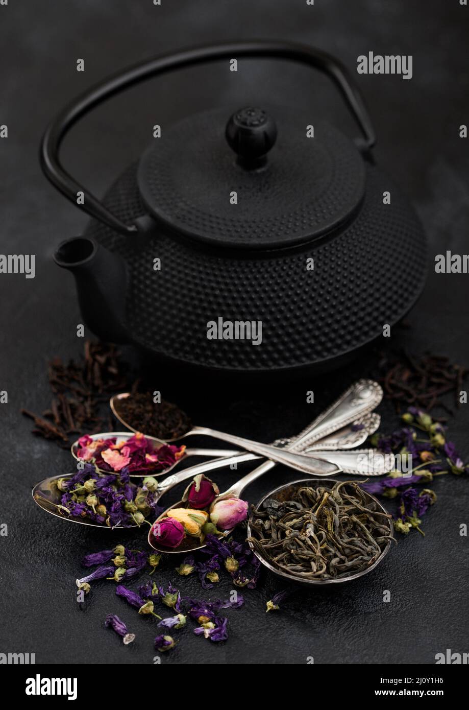 Chinese teapot with cup and spoons with various tea on black. Rose buds ...