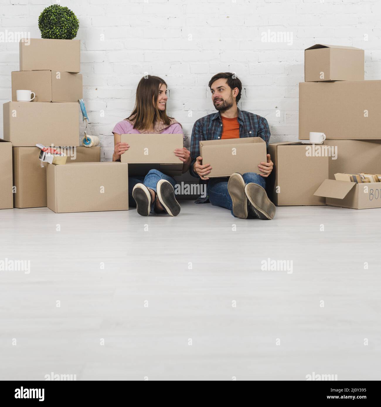 Young couple sitting floor holding cardboard boxes hand looking each ...
