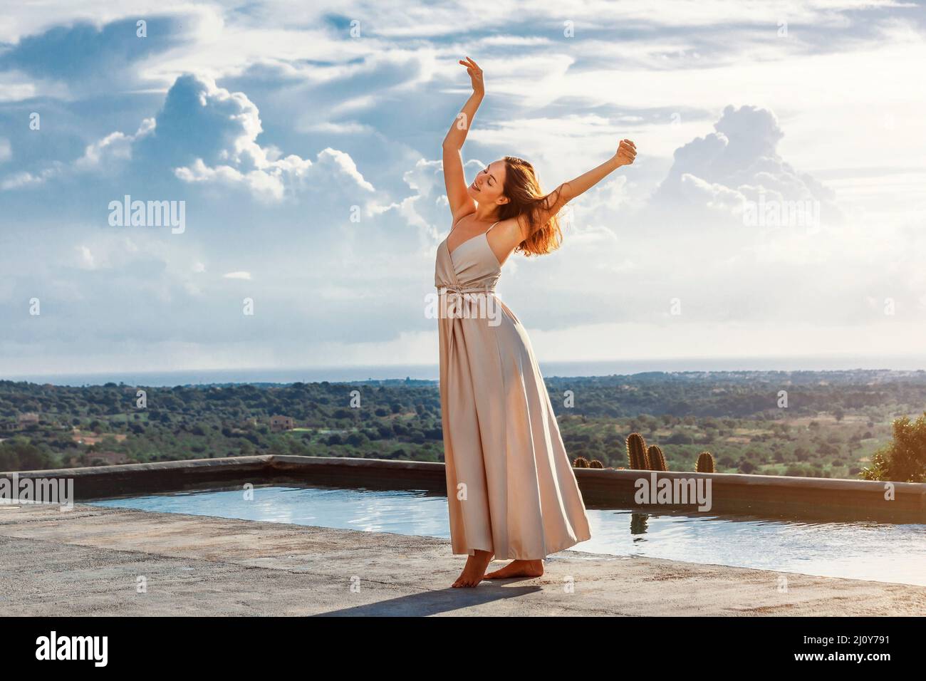 young brunette woman dancing next to a pool, wearing a cream white ...