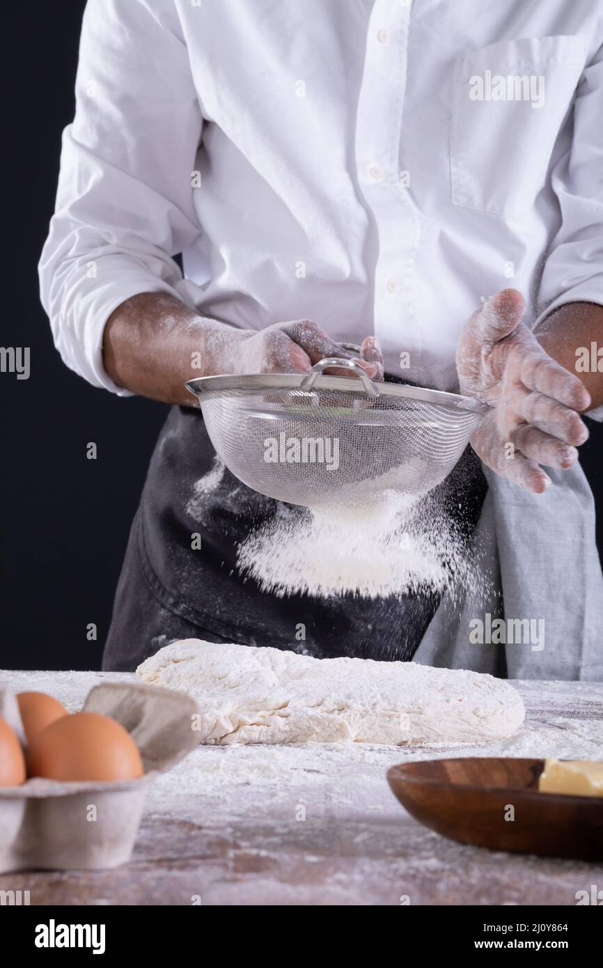 Midsection of african american male baker sprinkling flour with sieve ...