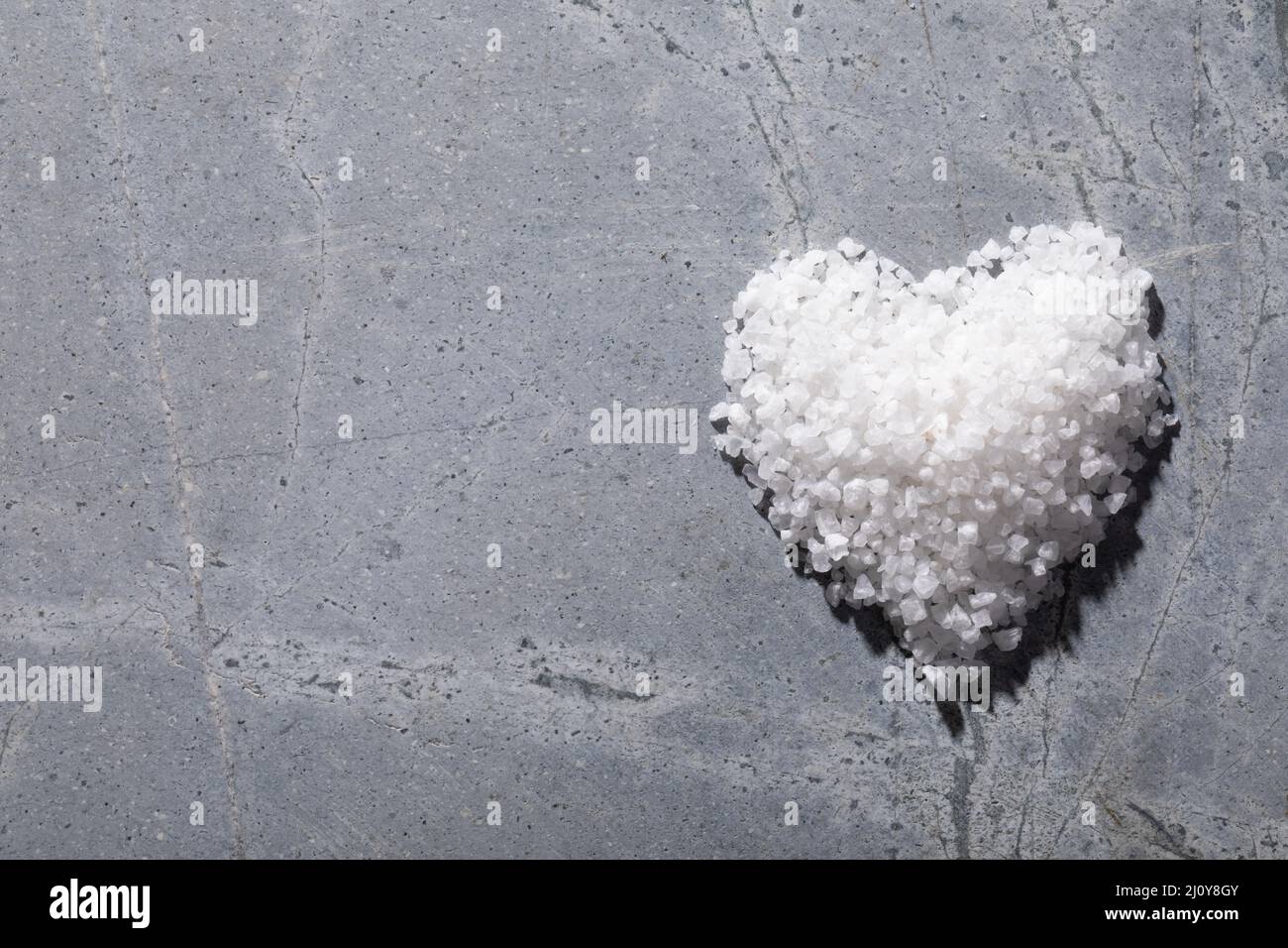 Overhead view of rock salt in heart shape pattern on gray table with ...