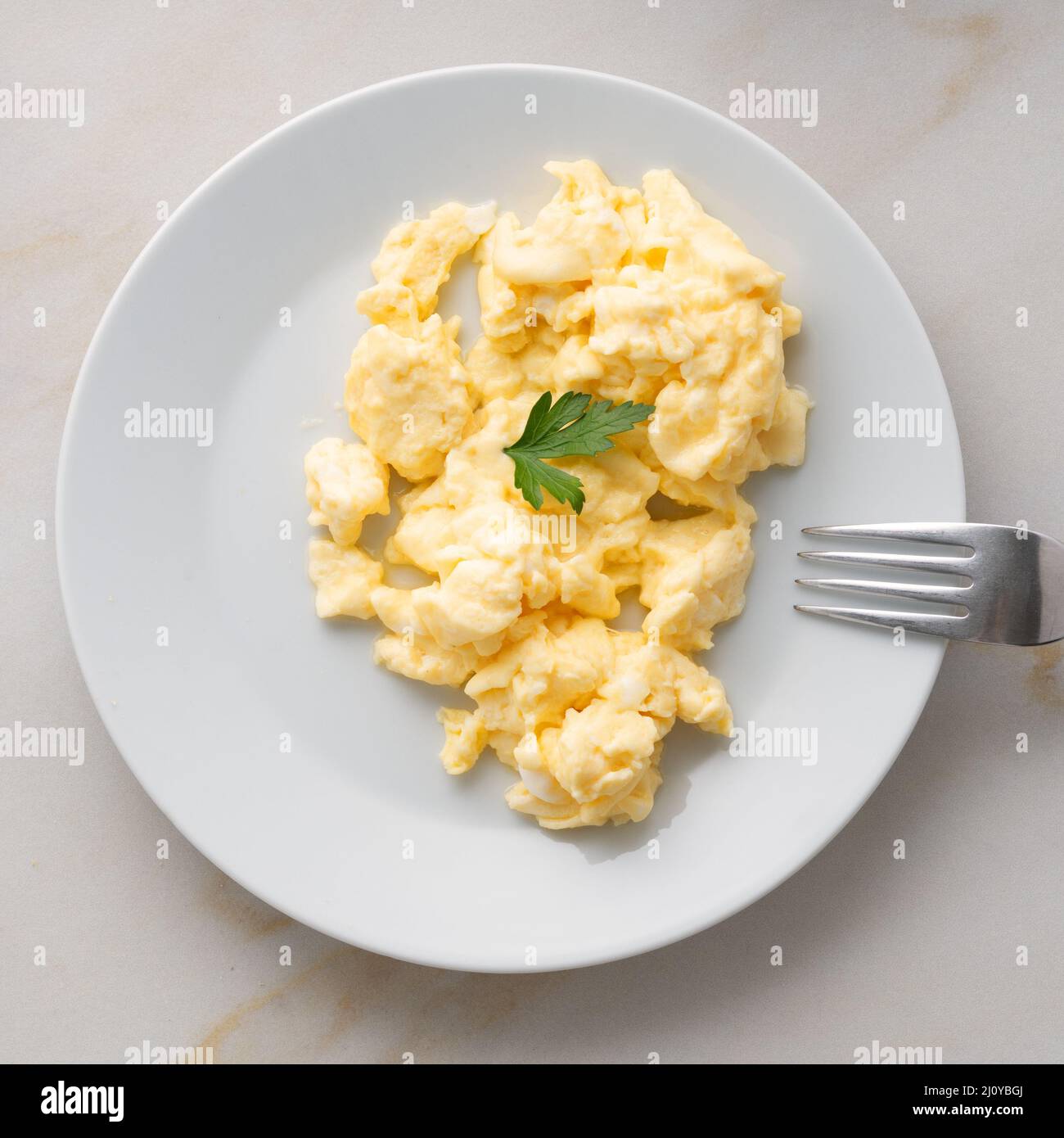 White plate with pan-fried scrambled eggs on white light background ...