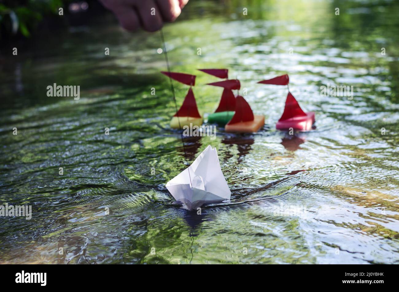 Sailboats made of kitchen sponges in pursuit of a white paper ship. Man ...