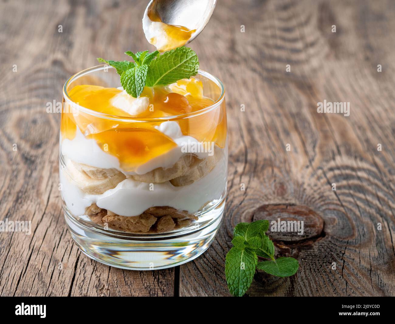 Healthy layered dessert with yogurt, banana, mango, cookie on wooden ...