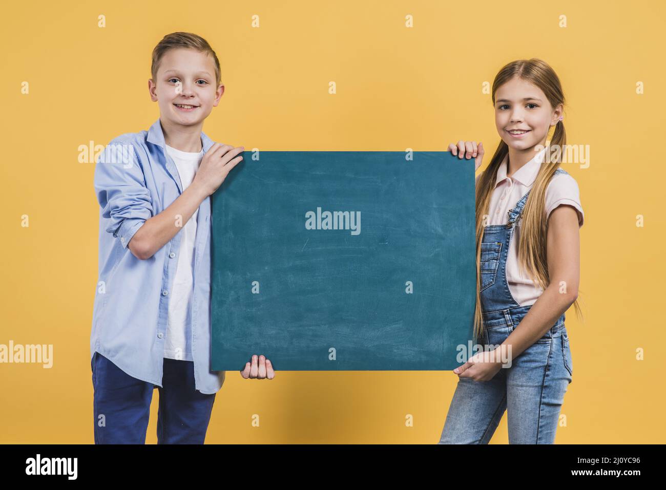 Boy girl holding green chalkboard against yellow backdrop. High quality ...