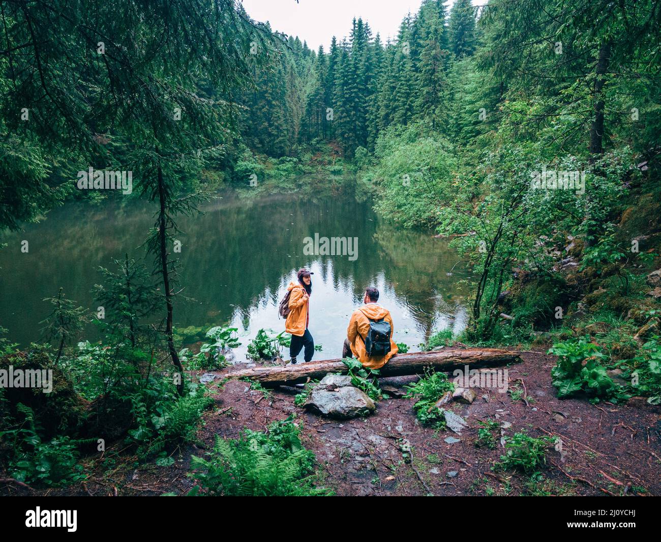couple hikers in yellow raincoat looking at mountain lake Stock Photo ...