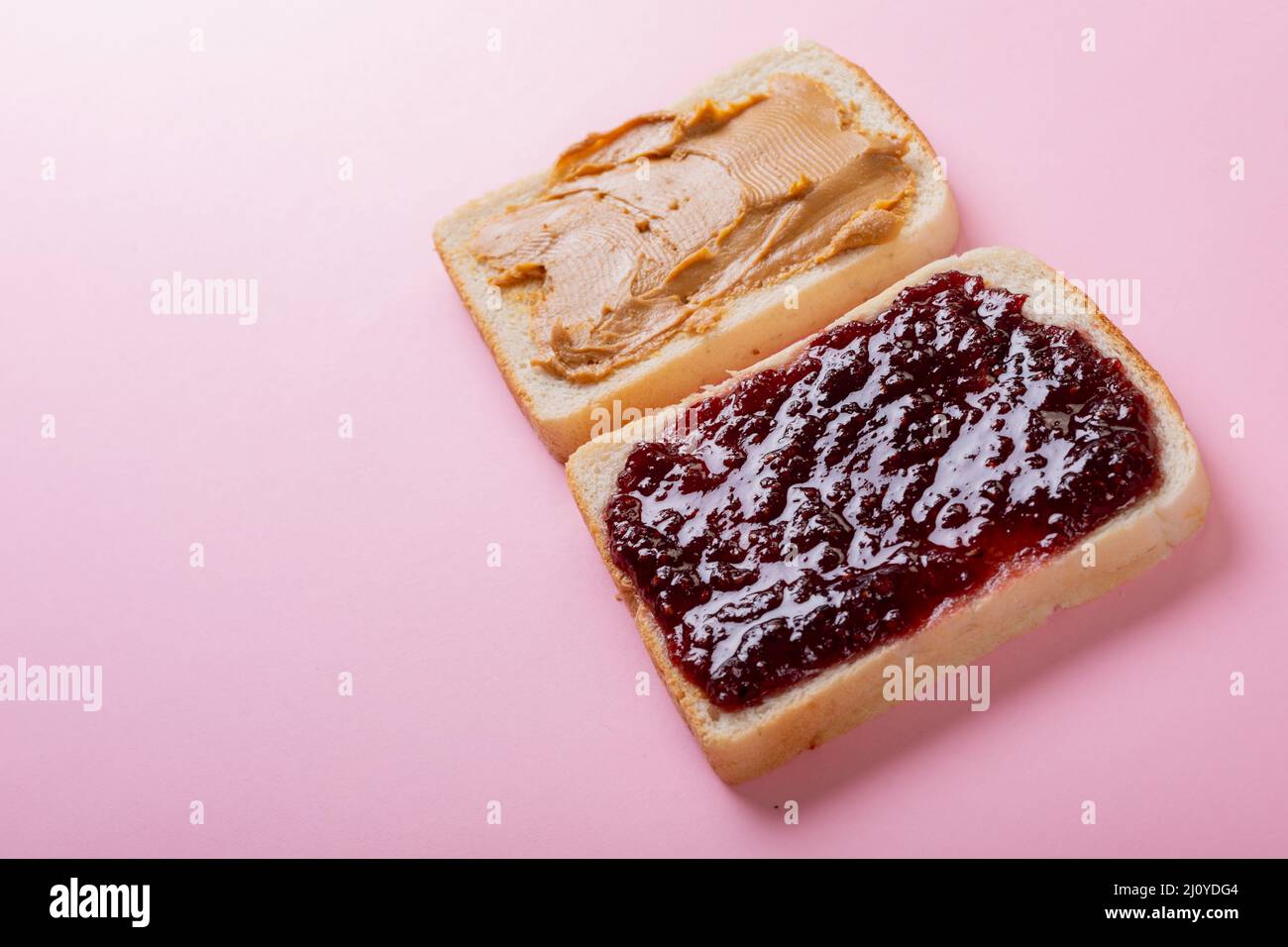 Close-up of peanut butter and preserves on bread slices over pink ...