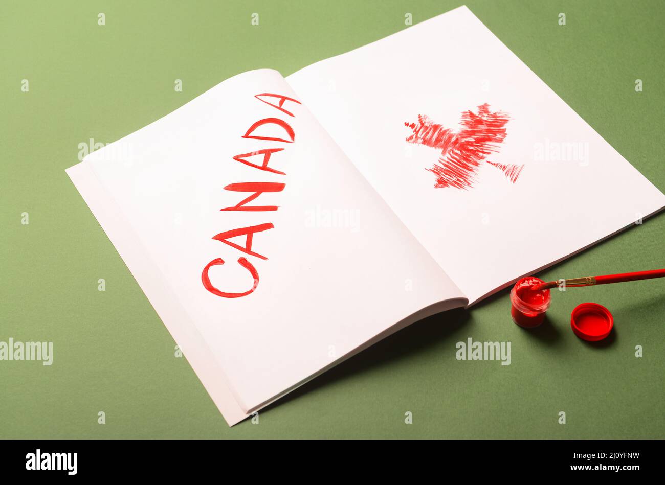 Open notebook with word CANADA, drawn maple leaf and paints on green ...