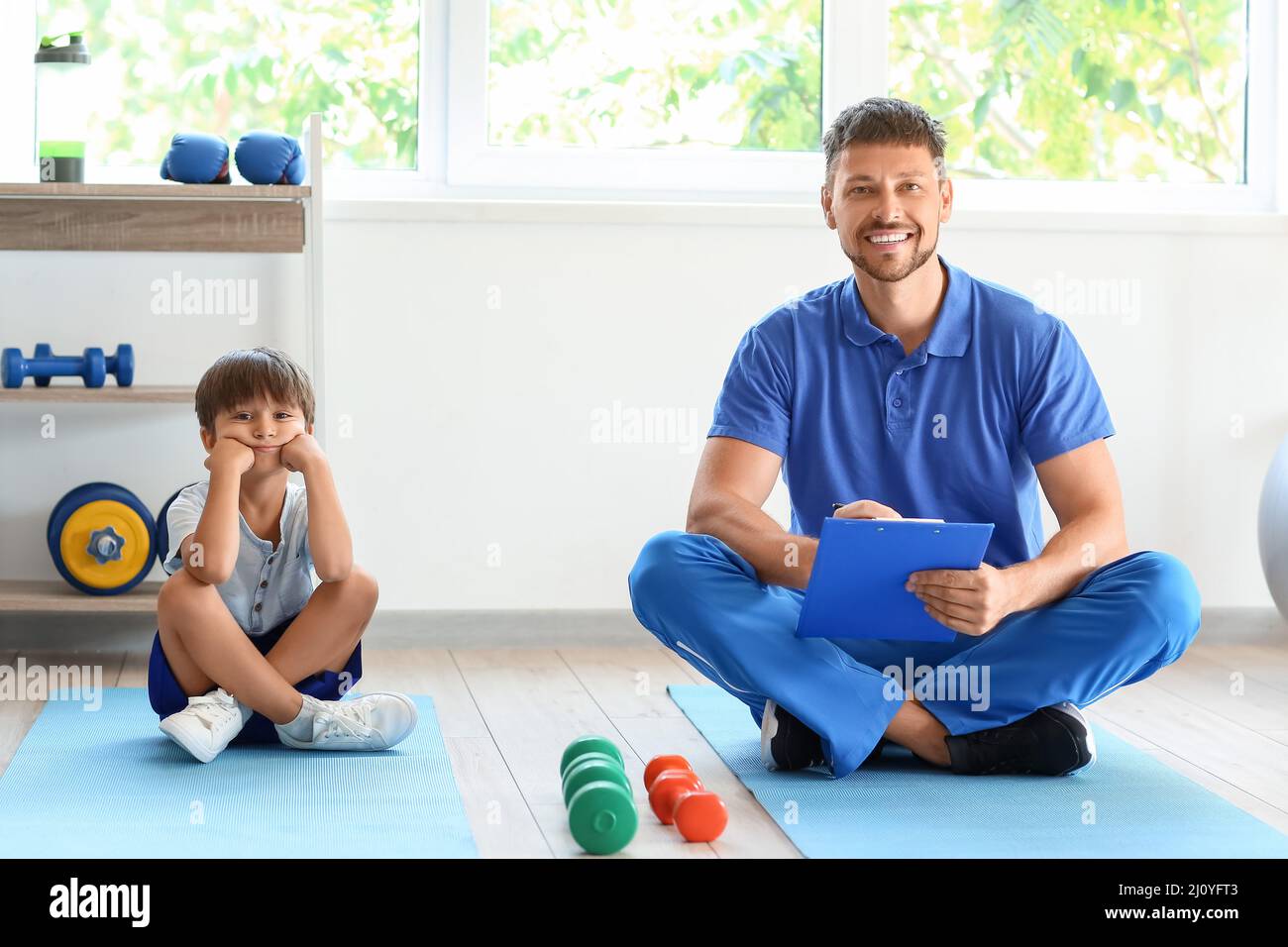 Male trainer with clipboard and little boy in gym Stock Photo - Alamy