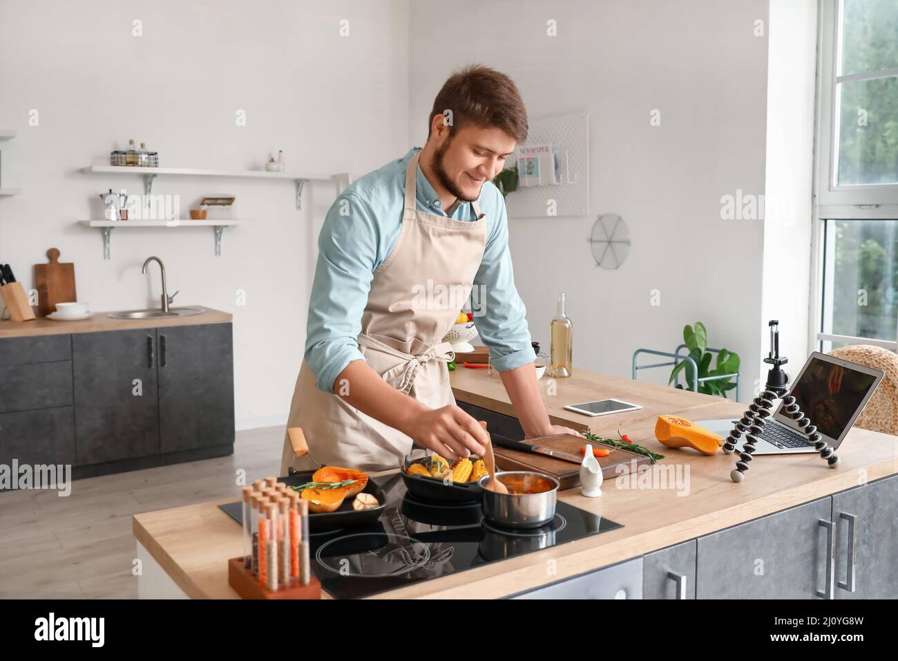 Young man cooking vegetables while following video tutorial in kitchen ...