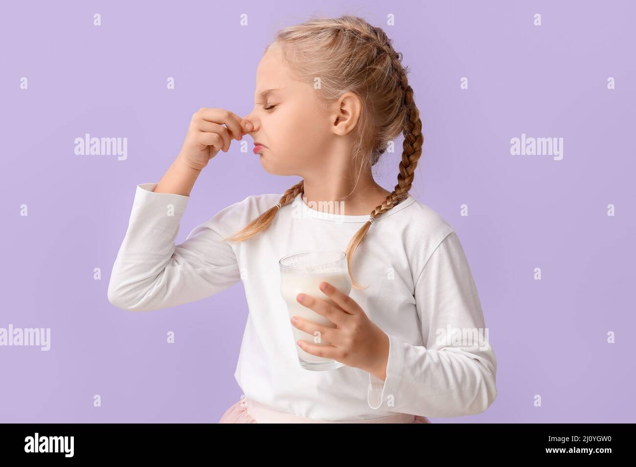 Cute little girl with glass of milk closing nose on lilac background ...