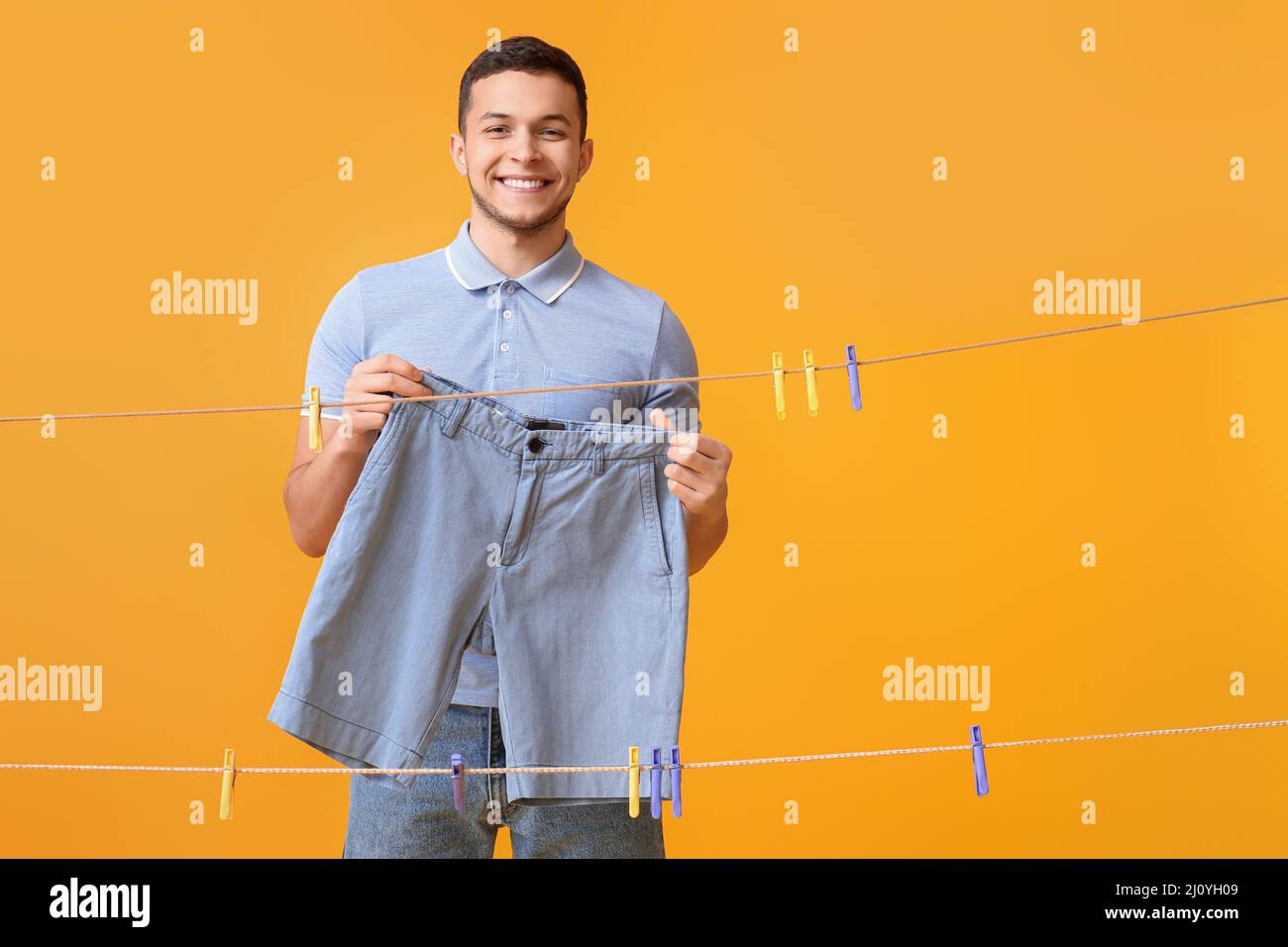 Young man hanging clean shorts with plastic clothespin on yellow ...