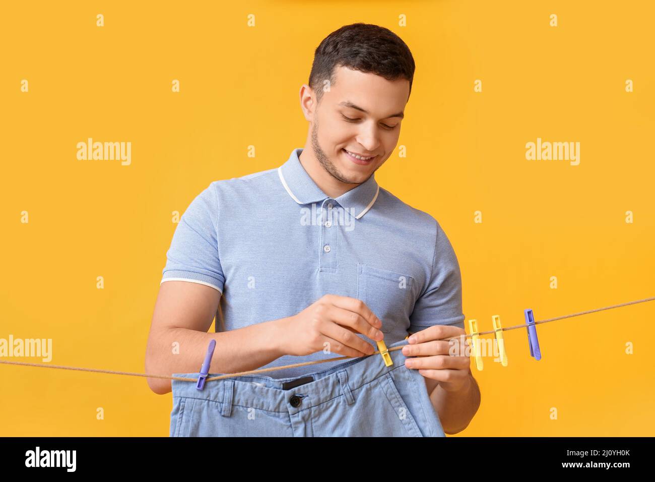 Young man hanging clean shorts with plastic clothespin on yellow ...