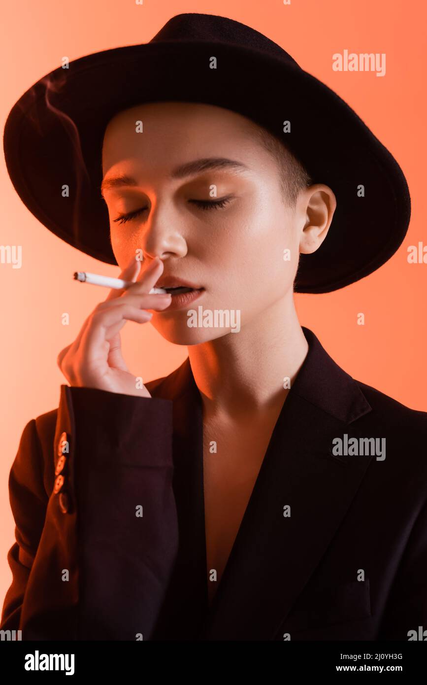 sensual and stylish woman with closed eyes smoking on coral background ...