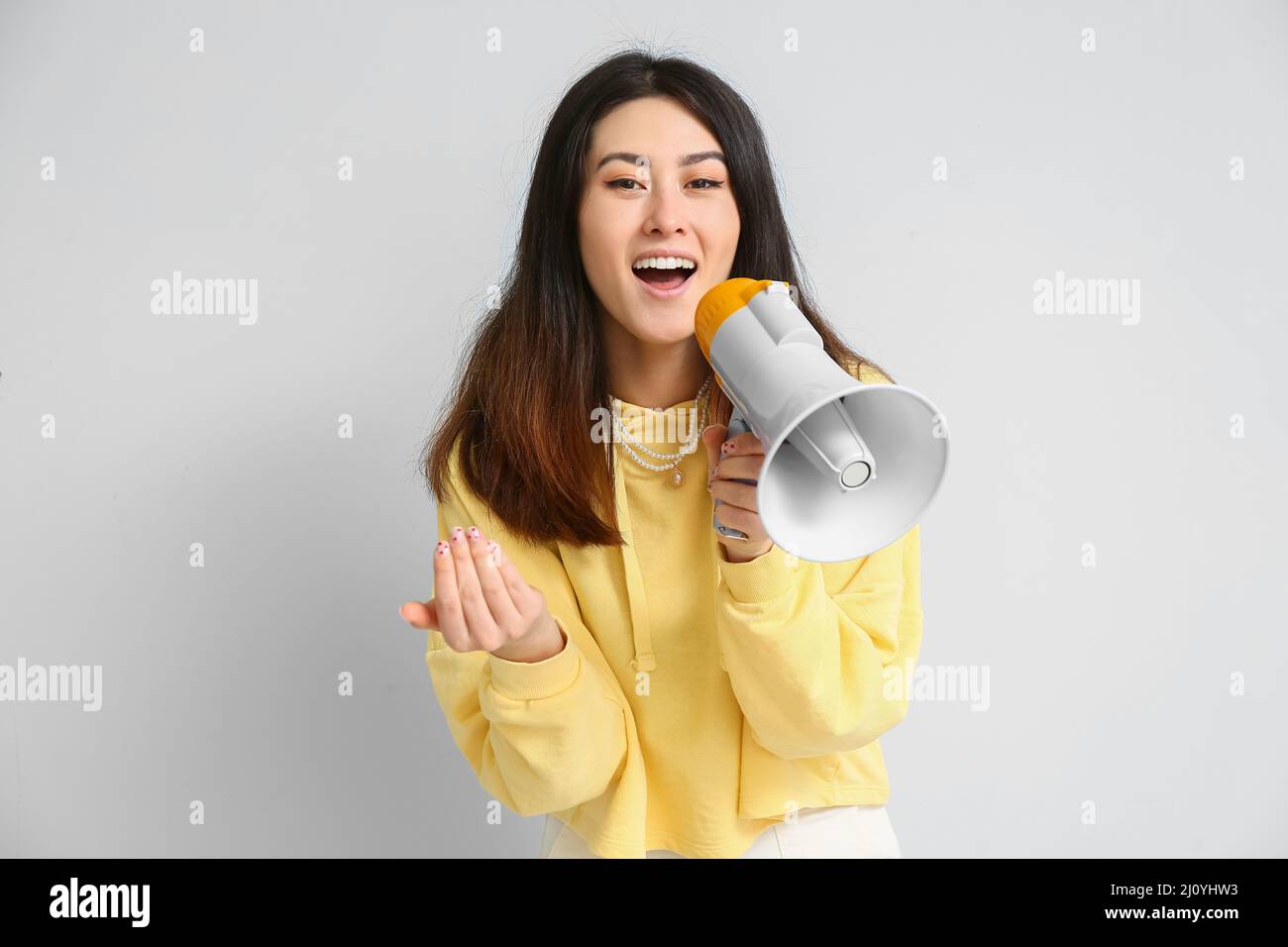 Young Asian woman with megaphone inviting viewer on light background ...