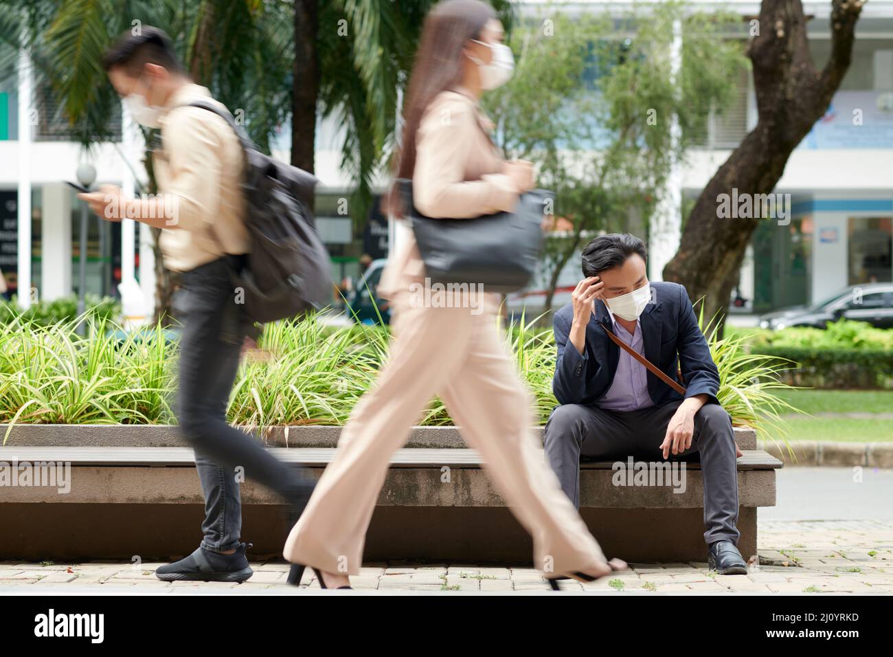 Stressed and tired entrepreneur sitting on bench in park when people ...