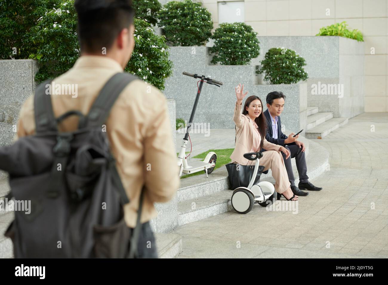 Young businesswoman sitting on steps with coworker and waving to ...