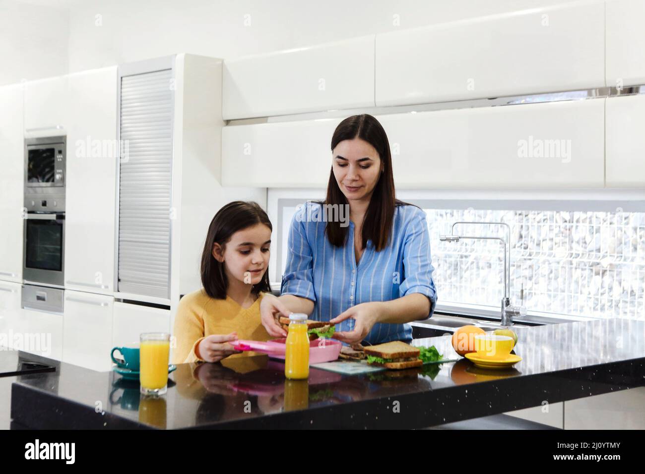 Cheerful ethnic mother making healthy lunch box with healthy food for ...